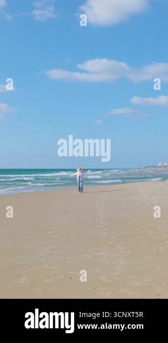 Vertical shot. young and slender brunette walks alone on sandy beach ...