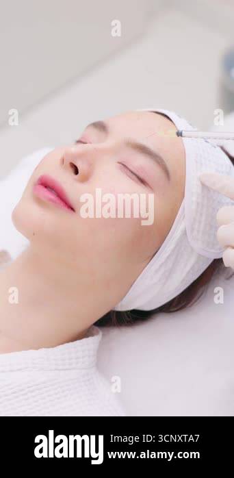 A close-up of a young Asian woman receiving a Botox or dermal filler ...