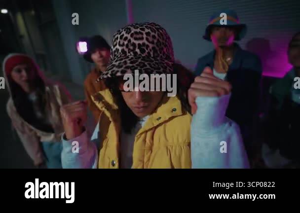 Confident young woman performs hip hop dance in neon-lit urban setting ...