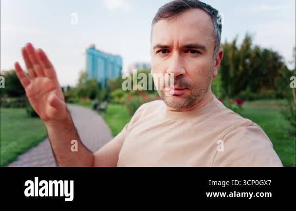 Man standing in a green city park, gesturing and speaking directly to ...