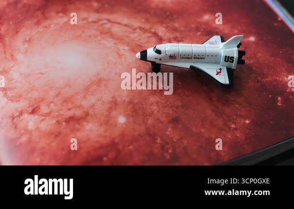 Close up of a miniature toy space shuttle placed on a reddish galaxy ...