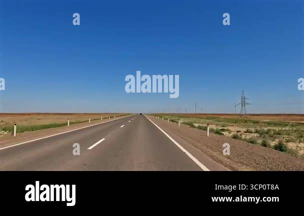 A long empty road with a blue sky overhead. There are power lines along ...