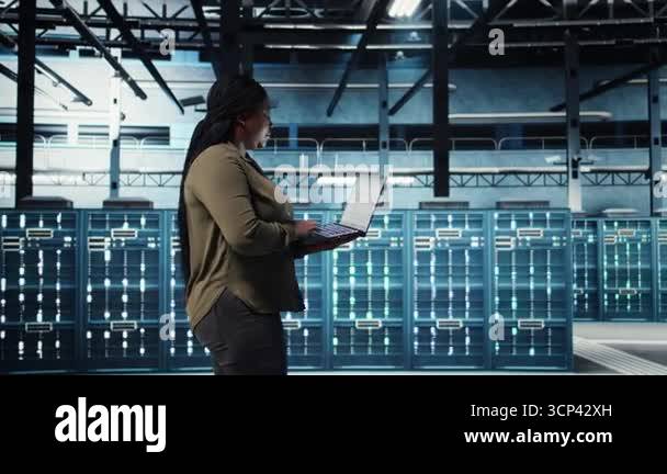 Engineer walks in server hub, using laptop to upgrade rigs for increase in clients workload ...