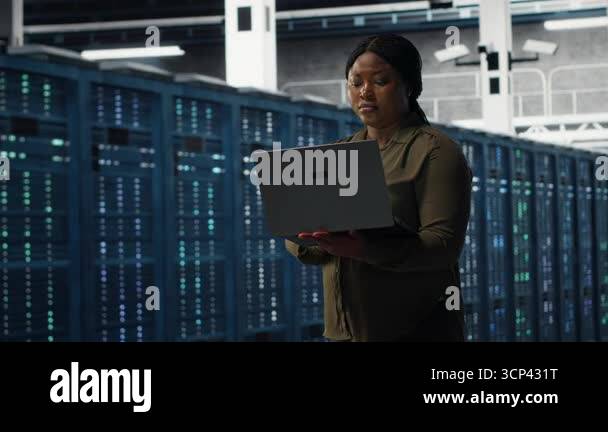 Smiling engineer walking in data center with laptop, checking hardware ...