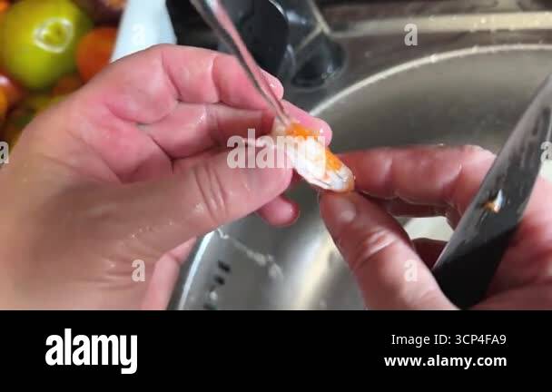 A woman is deveining and peeling shrimp tails in her kitchen. She ...