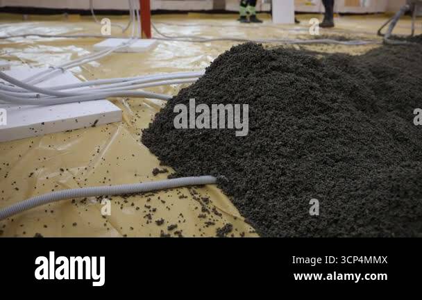 Indoor construction scene with workers spreading and leveling liquid foam concrete and cement ...