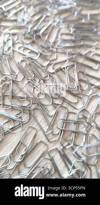 A macro shot of metal paper clips scattered across a light wood surface ...