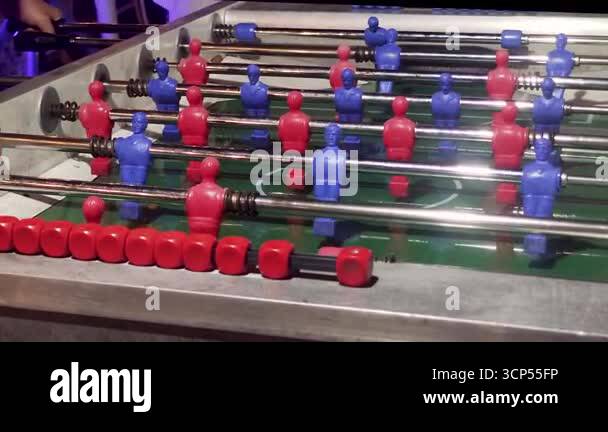 Hands moving foosball rods during a match, with red and blue players ...