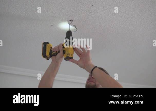 A man drills holes in the ceiling to install a chandelier during a home ...