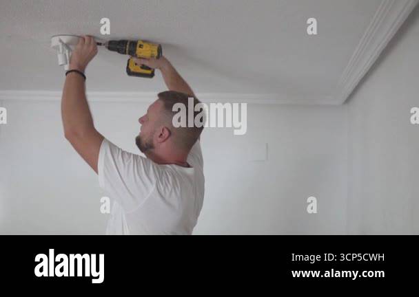 A man installs a new chandelier by drilling into the ceiling during a ...