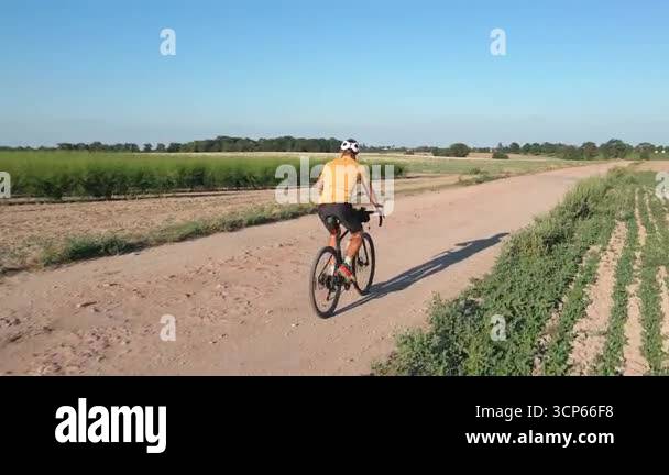 Cyclist wearing helmet and sportswear riding gravel bike on a dirt road ...