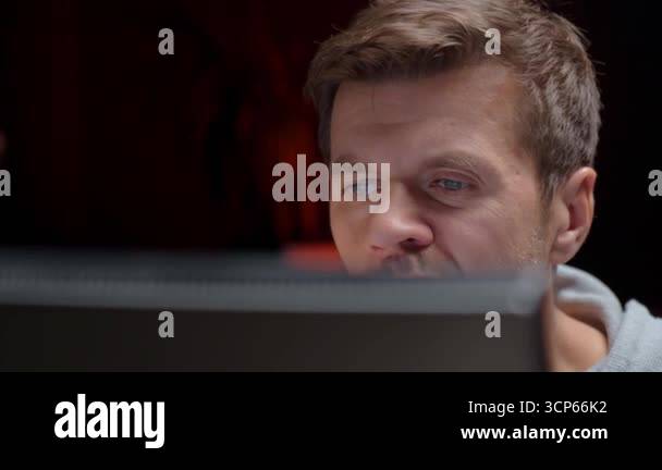 Tired man working at computer in dark room. Close up of man eyes ...