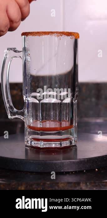 Tomato and clam juice being poured into a large beer mug with a spicy ...