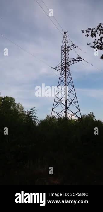 A tall power pylon dominates the frame, silhouetted against a sky with ...
