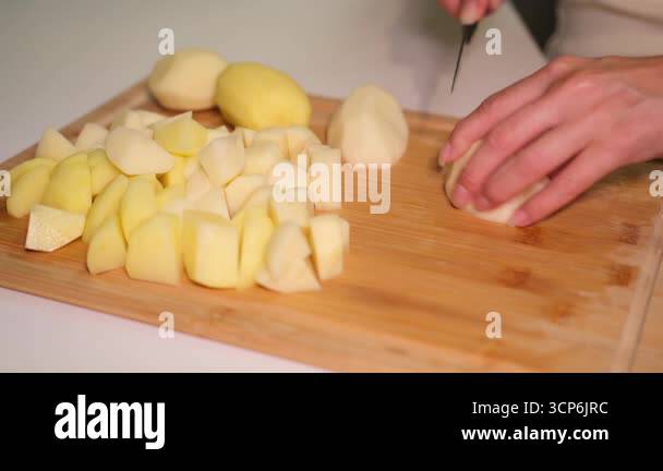 A closeup view of hands skillfully chopping fresh potatoes on a rustic ...