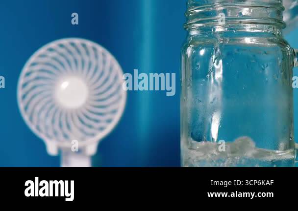 Pouring ice water with desk fan on cool blue background close up zoom ...
