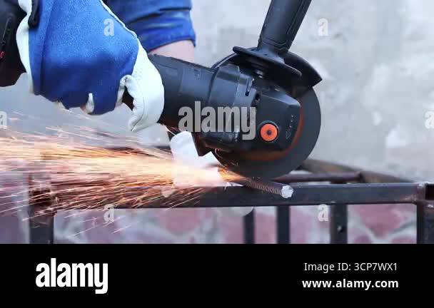 Close-up of an angle grinder cutting rebar. Female hands in work gloves ...