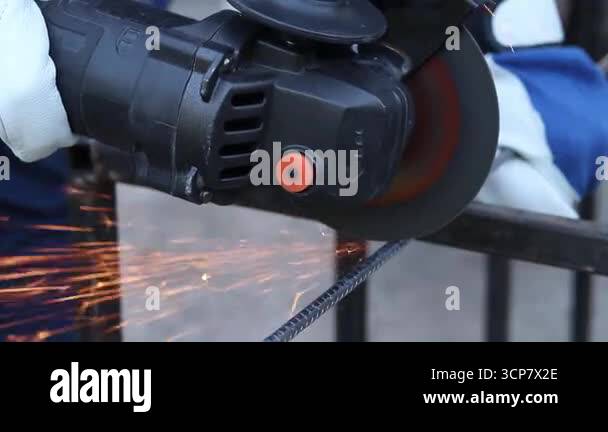 Close-up of an angle grinder cutting rebar. Female hands in work gloves ...