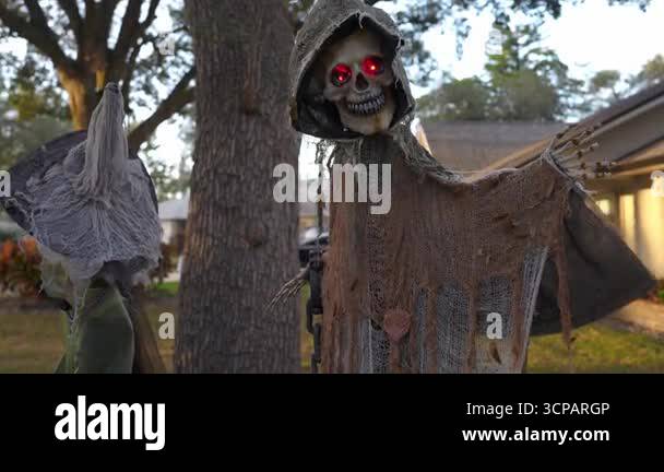 Tattered hooded skeleton with glowing red eyes stands in a suburban ...
