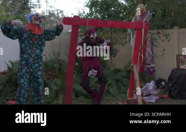 Scary clown and jester decorations stand in a backyard beside a red ...