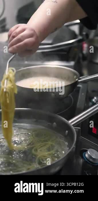 Vertical video. Cooking spaghetti. Noodle meal. Chef hand adding pasta ...