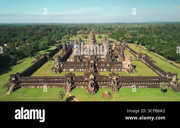 Dynamic aerial fly away footage of Angkor Wat temple complex in Cambodia, surrounded by lush ...