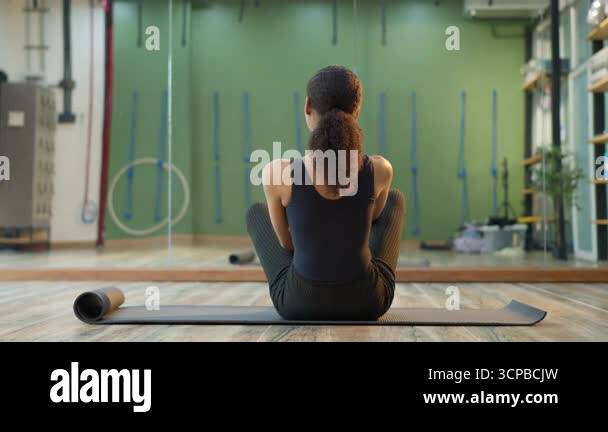 Woman sitting on mat in yoga studio practicing seated twist pose for ...