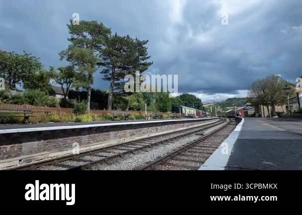 A vintage diesel train stops at an old station under stormy, cloud-filled skies, captured in a ...