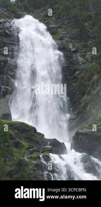 Vertical slow-motion of a large alpine waterfall thundering down rocky ...