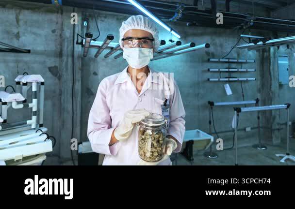 Scientist in protective gear holding a specimen jar in an industrial ...