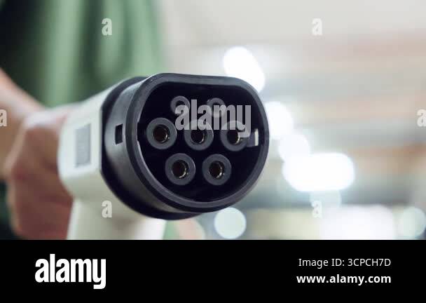 Close-up of a person holding an electric vehicle charging connector ...