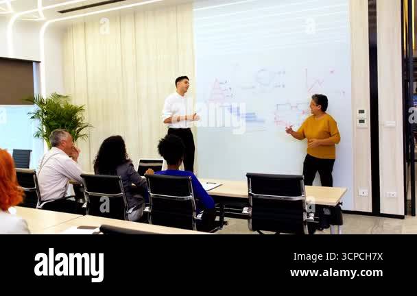 Diverse colleagues in a modern conference room applaud as two coworkers lead a whiteboard ...