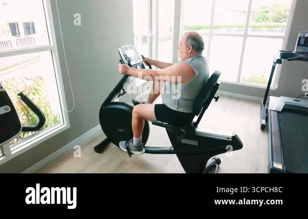 Senior individual exercises on recumbent stationary bike in bright gym ...
