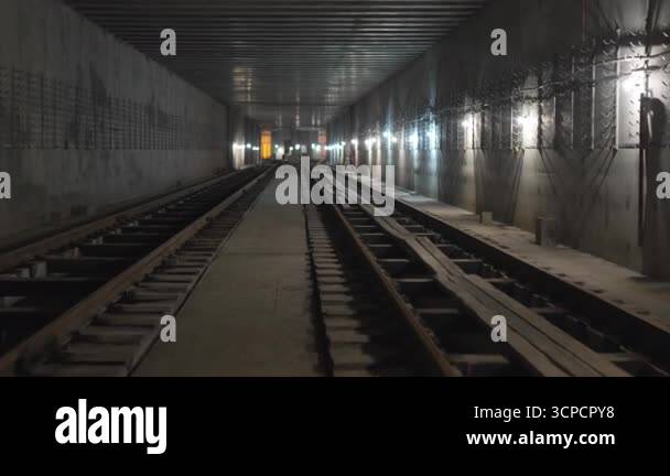 Rails stretch through dim tunnel lined with hooks. Wires cling to walls ...