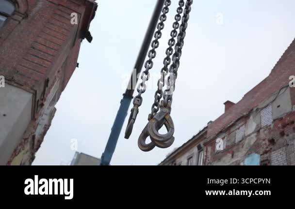Metallic crane hooks swing between fragile aged stone walls under ...