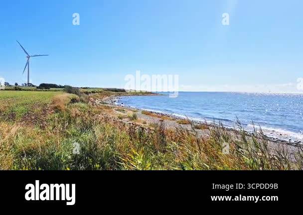 A stunning shoreline view featuring a wind turbine, lush greenery, and ...