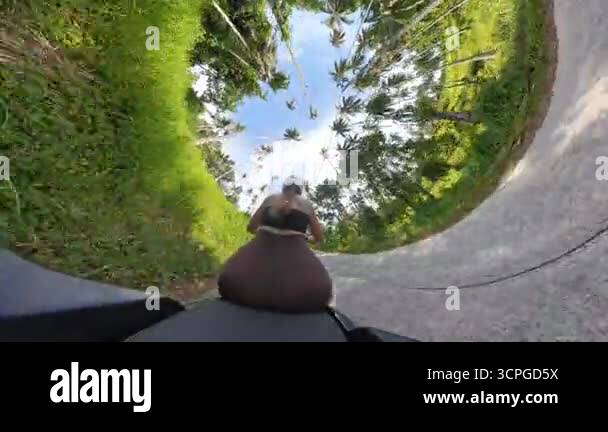 Woman driving scooter through lush tropical road with curving pavement ...