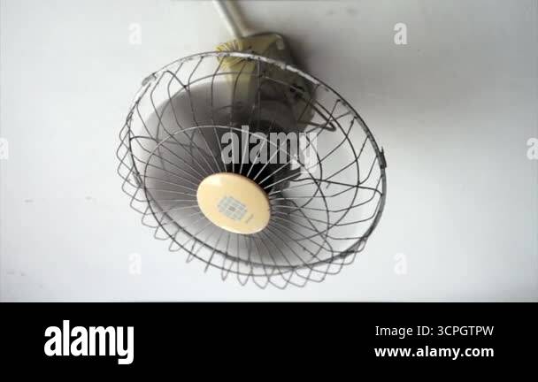 An old electric ceiling fan with a protective grill, designed for ...