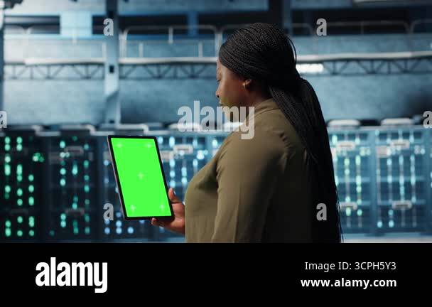 Data center specialist monitors data center metrics on green screen tablet to enhance ...