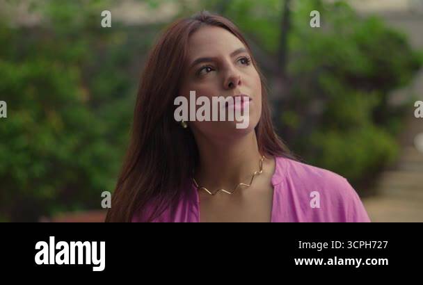 Latina woman glancing upward with soft expression, standing in backyard ...