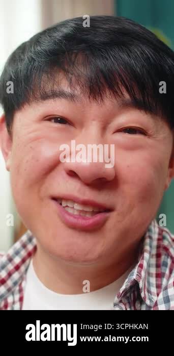 Asian man at home laughs, gesturing during POV video call, enjoying lively talk with friend ...