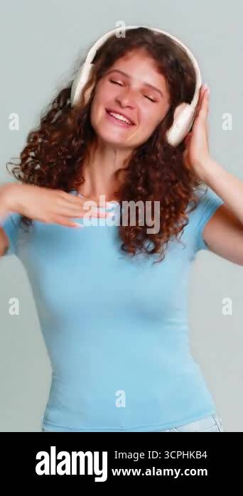 Young woman happily putting on headphones, dancing joyfully, smiling ...