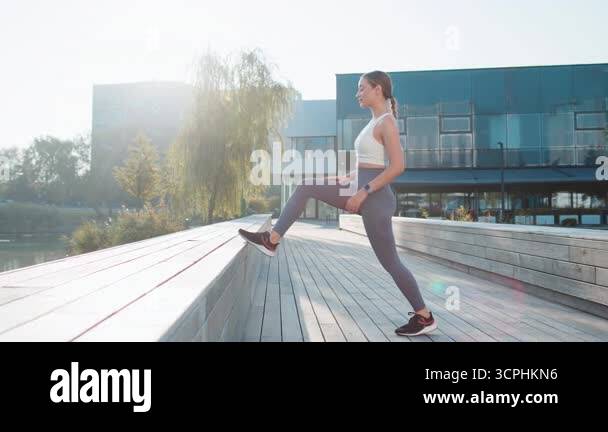 Side view of athletic young woman runner stretching legs before jogging ...