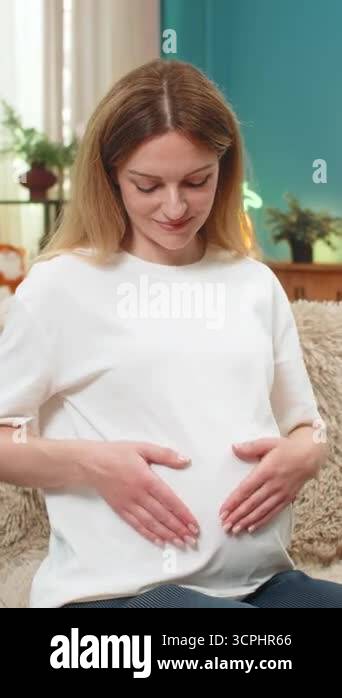 Pregnant middle-aged woman at home forms heart above belly eyes shine ...
