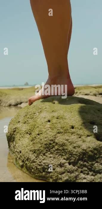Vertical video. Barefoot Person Standing on Mossy Rock by Shallow Water ...