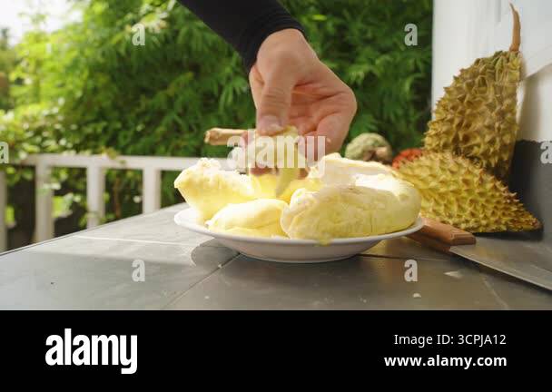 Hand Pinching Small Soft Piece of Durian Flesh Above White Plate With ...
