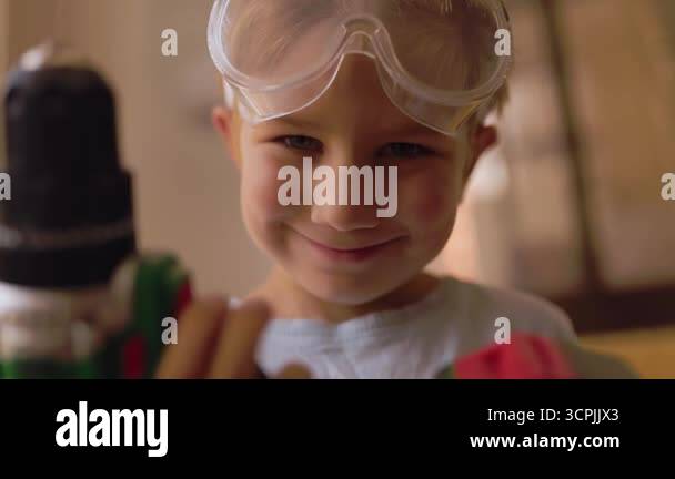 Proud young boy wearing safety goggles holds a toy power drill and ...