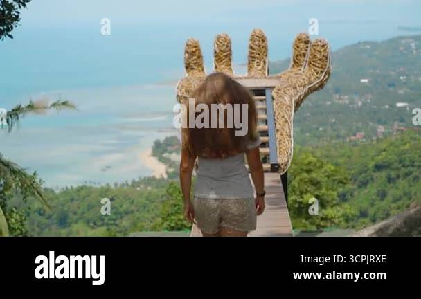 Woman walking on large wooden hand shaped viewpoint over sea and green ...