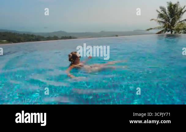 Woman Floating on Back in Blue Infinity Pool with Forest Hills and ...