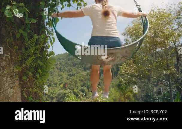 Woman Swinging Over Green Valley Facing Mountain Range with Arms ...